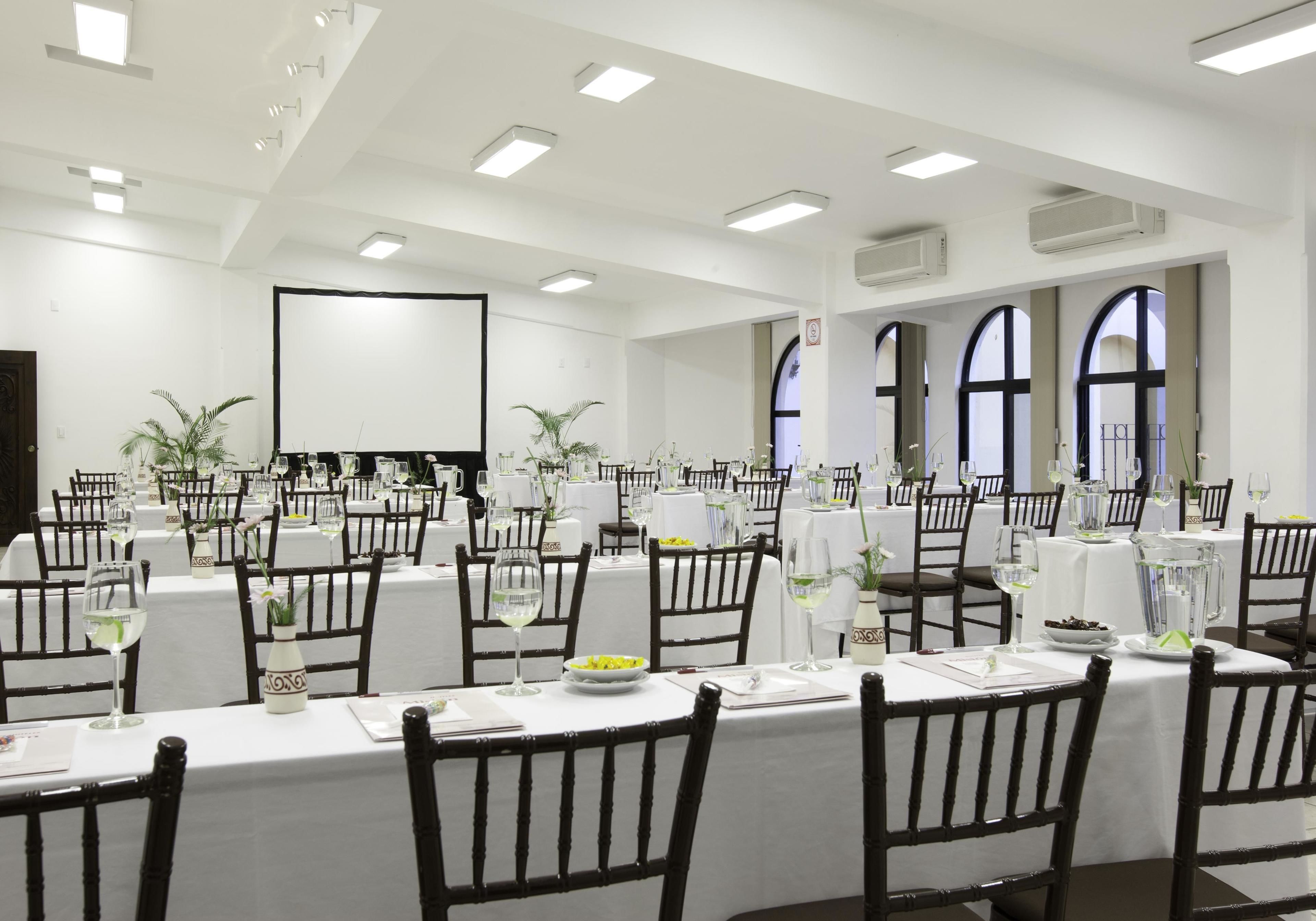 Uma sala de conferência com várias mesas preparadas para uma reunião, equipada com cadeiras, mesas e telas de apresentação.