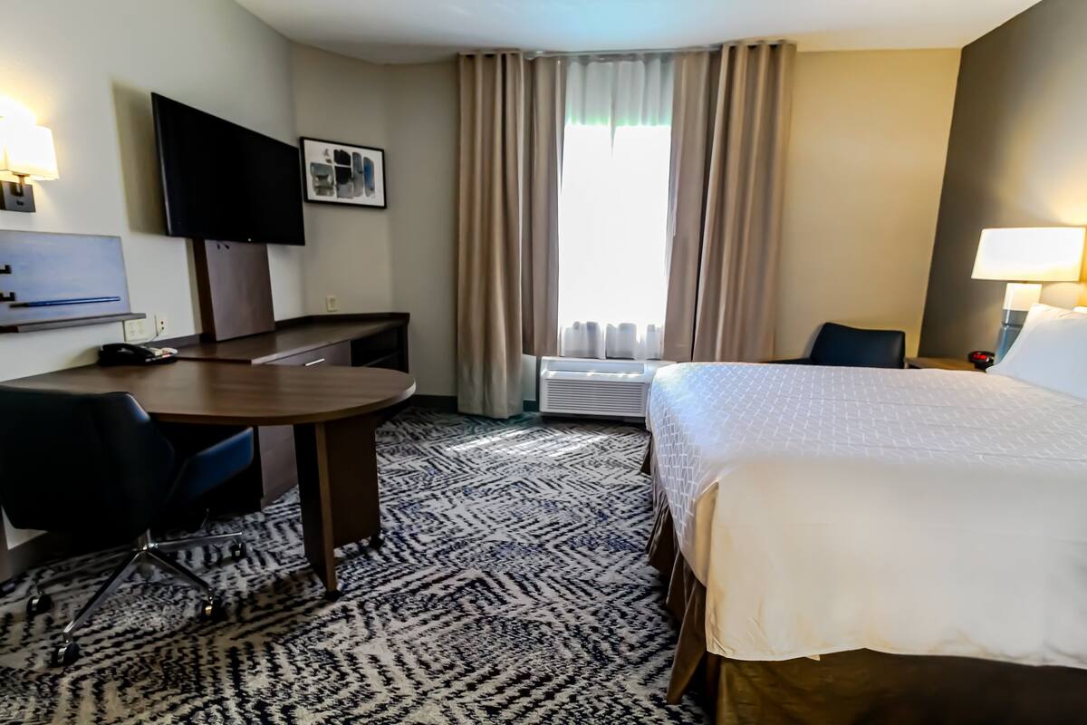 Quarto de hotel com cama, escrivaninha, cadeira, televisão e janela com cortinas.