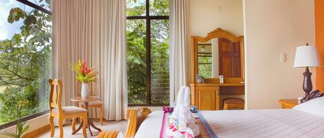 Quarto de hotel com cama, escrivaninha, cadeira, janela com cortinas, espelho e mesa de cabeceira com abajur.