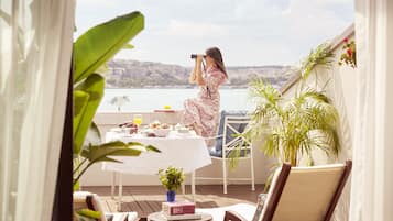 Mulher fotografando em uma varanda com uma mesa posta para o chá, com vista para a água e colinas.