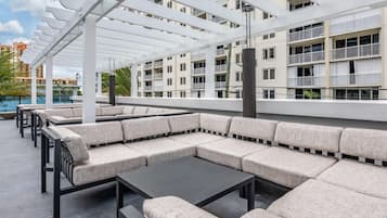 Uma área de lounge no terraço com assentos externos e uma piscina ao fundo.