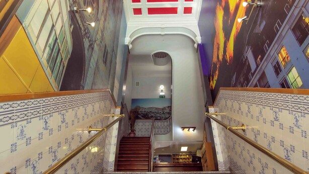 Uma escadaria imponente com teto vermelho e um mural retratando uma paisagem urbana.