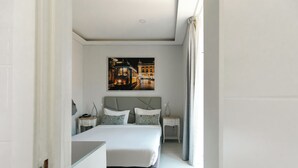 Quarto de hotel moderno com uma cama grande, uma mesa de cabeceira e um quadro na parede retratando uma rua da cidade à noite.