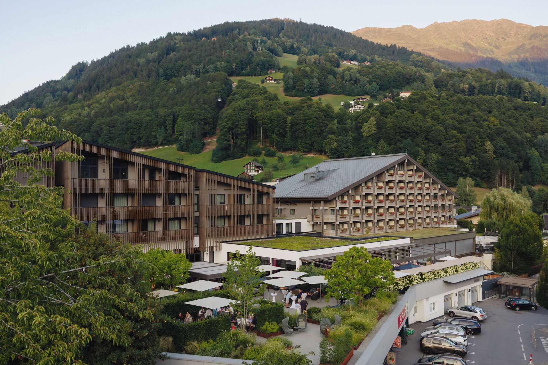 Um hotel com vários edifícios, área de estacionamento e montanhas ao fundo.