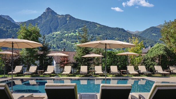Uma área de piscina com espreguiçadeiras e guarda-sóis, rodeada por montanhas.