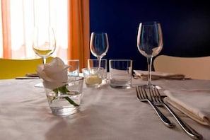 Mesa de jantar posta com taças de vinho, um copo de água com uma flor, uma vela e talheres.