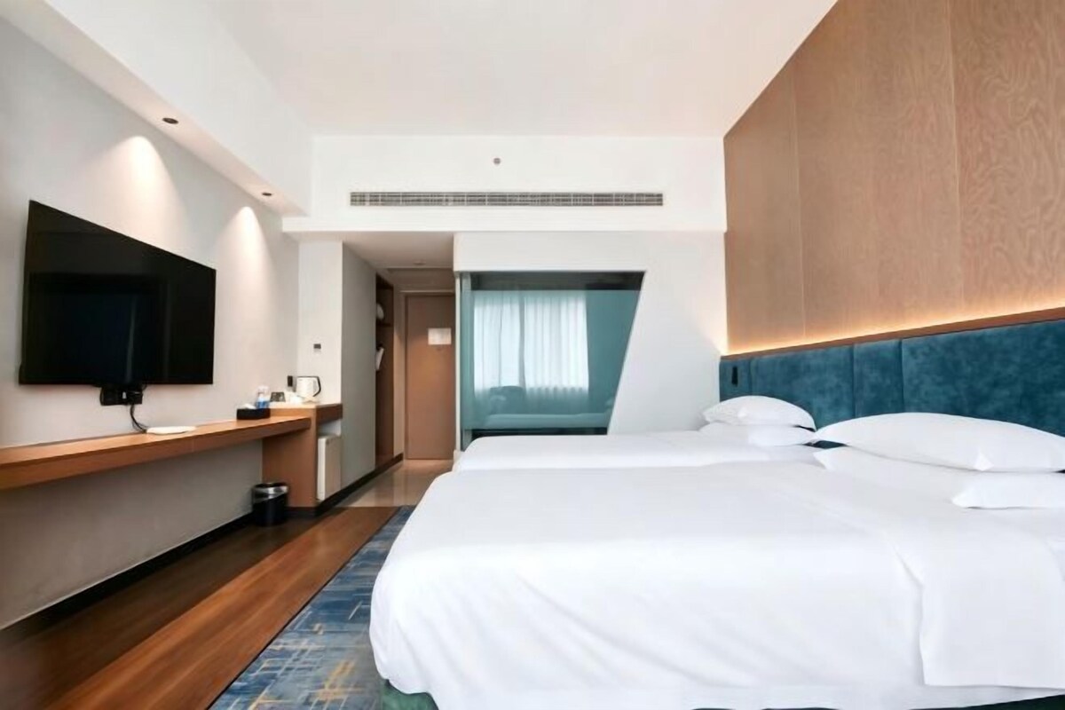 Quarto de hotel com uma cama grande, televisão fixada na parede e piso de madeira.
