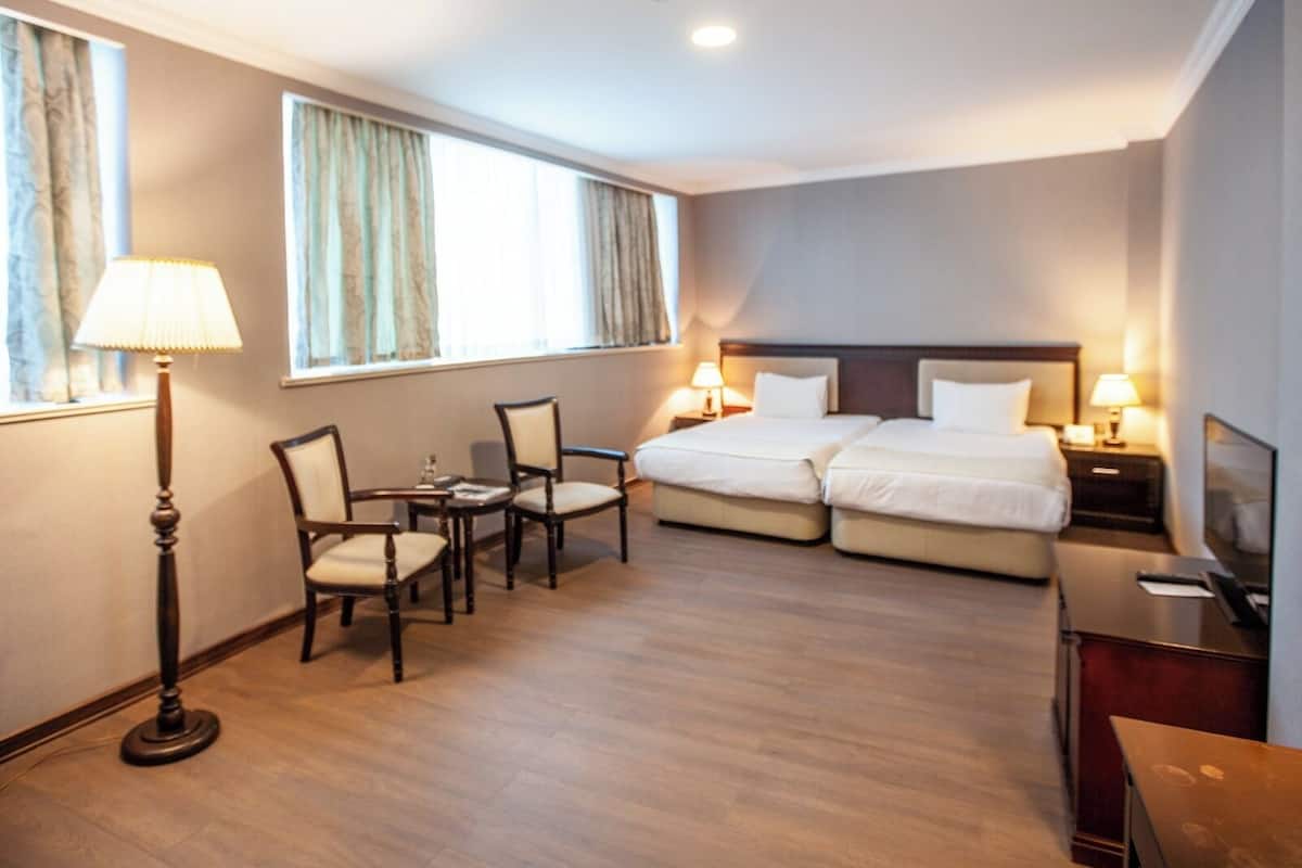 Quarto de hotel com duas camas, uma escrivaninha, uma cadeira, um abajur e uma televisão.
