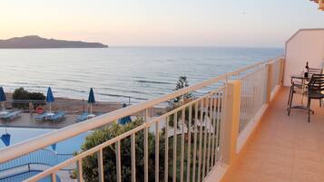 Uma varanda com vista para o mar, uma mesa com cadeiras e espreguiçadeiras.