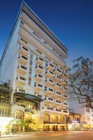 Hotel de vários andares com varandas, entrada coberta e vista para a rua.