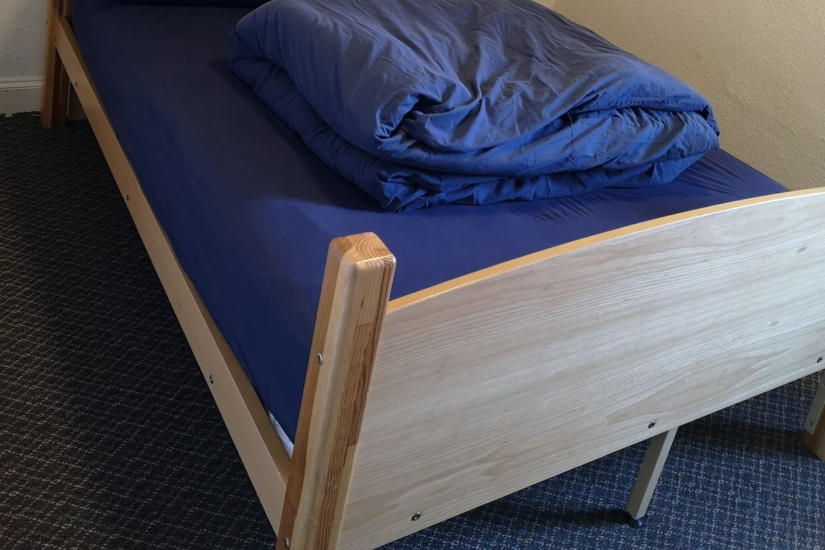 Uma cama de solteiro com estrutura de madeira, roupa de cama azul e duas mesas de cabeceira com abajures.