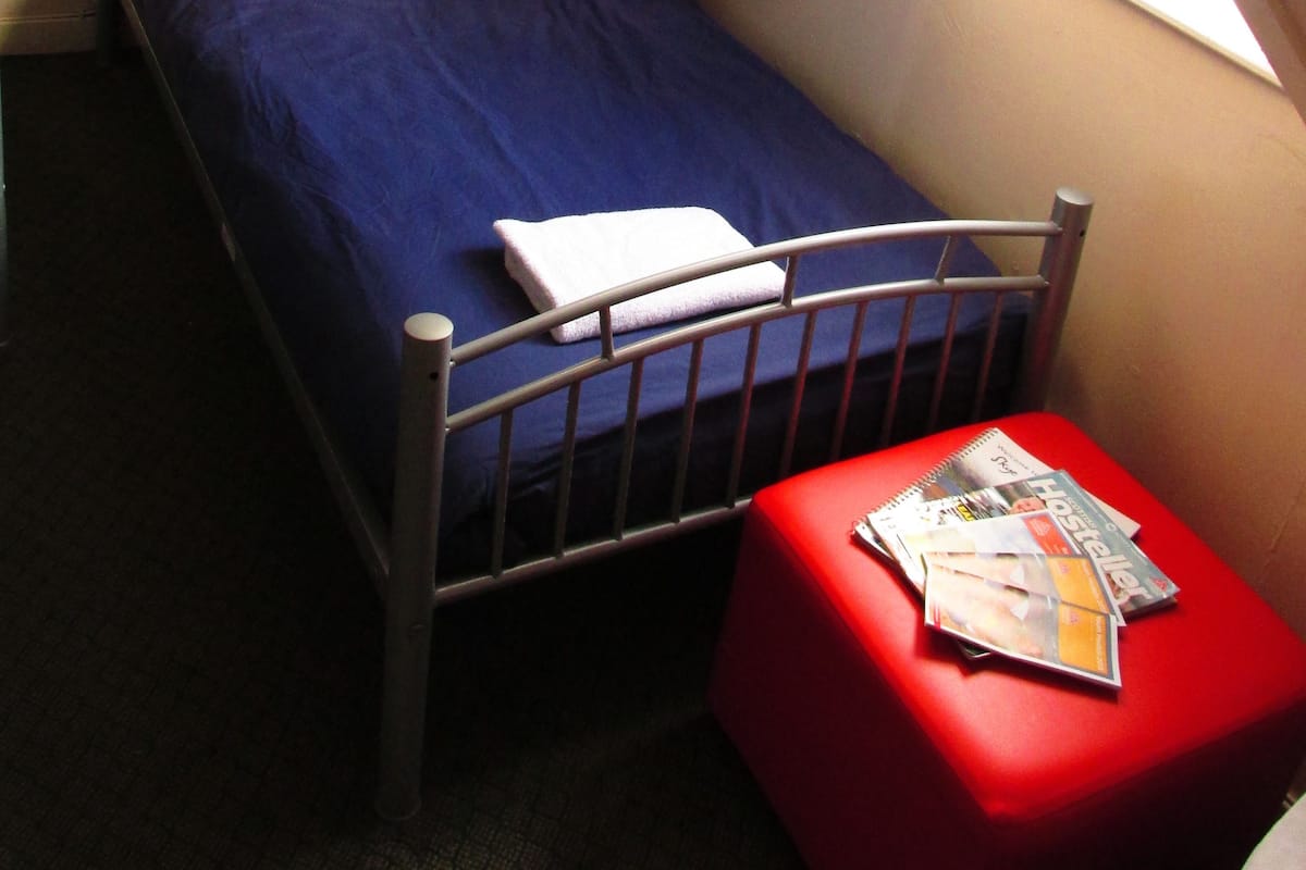 Quarto pequeno com cama de solteiro, teto inclinado e claraboia.