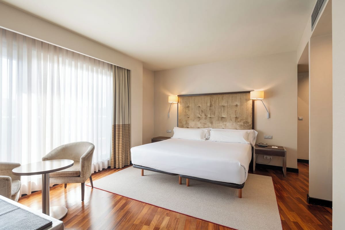 Quarto de hotel com uma cama grande, uma escrivaninha, uma cadeira e uma janela com cortinas.