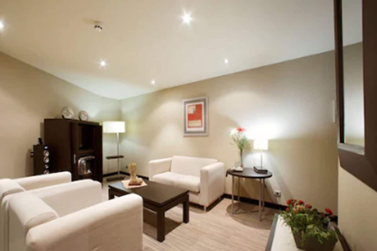 Uma sala de estar moderna com sofá, poltronas, mesa de centro, mesa lateral com abajur, um pequeno armário e uma planta em vaso.
