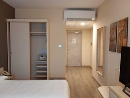 Quarto de hotel com cama, escrivaninha, guarda-roupa e ar condicionado.