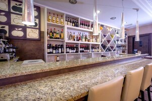 Uma área de bar com bancadas de granito, banquetas e prateleiras repletas de garrafas diversas.