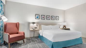 Quarto de hotel com cama, uma cadeira, escrivaninha e parede com quadros.