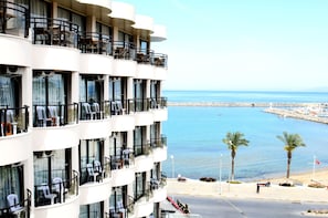 Um hotel com vários andares, varandas, vista para o mar e uma praia ao fundo.