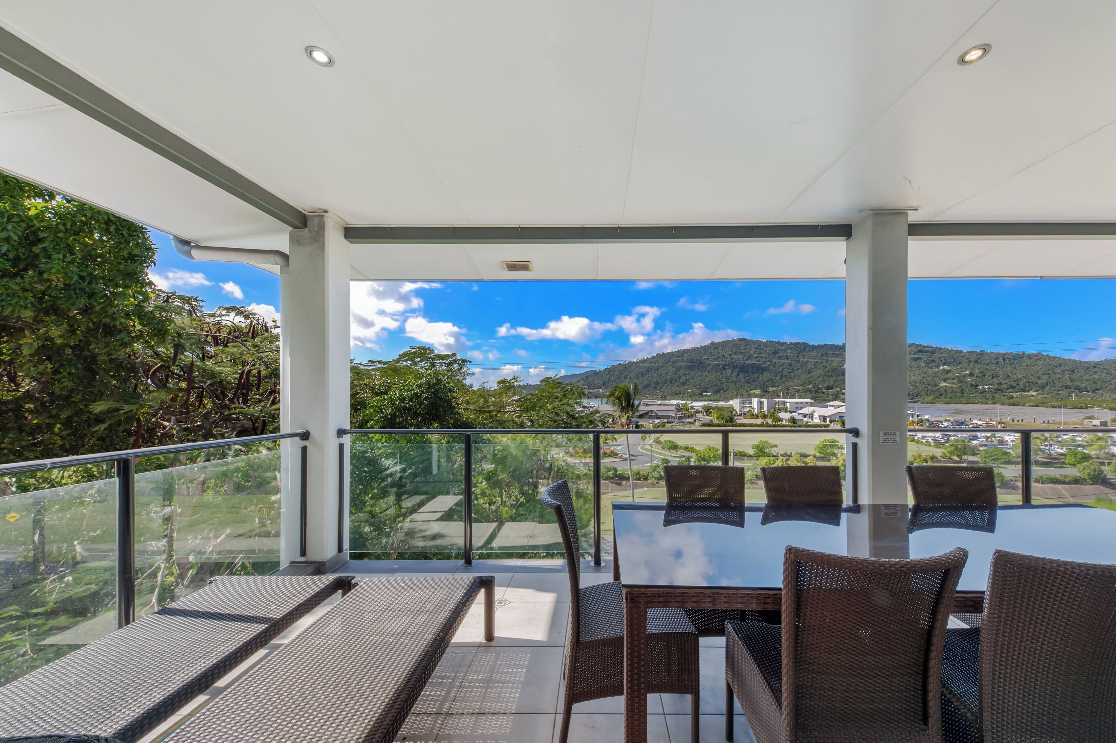 Uma área de estar coberta ao ar livre, com mesa e cadeiras, com vista para uma paisagem pitoresca com colinas e céu claro.