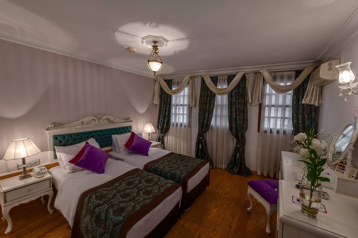 Quarto de hotel com duas camas, uma toucador com espelho e uma mesa com abajur.