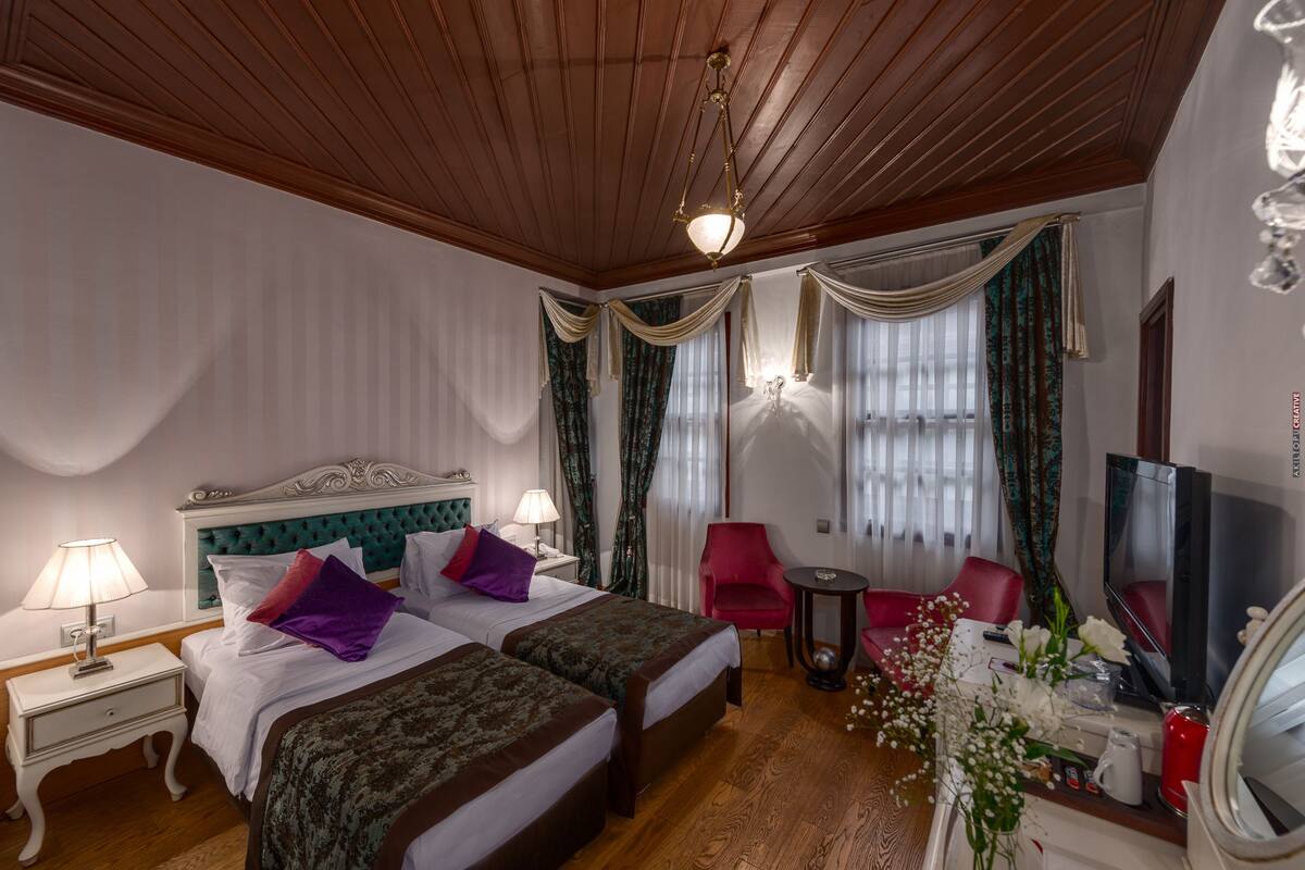 Quarto de hotel com duas camas, televisão, mesa pequena e uma cadeira vermelha.