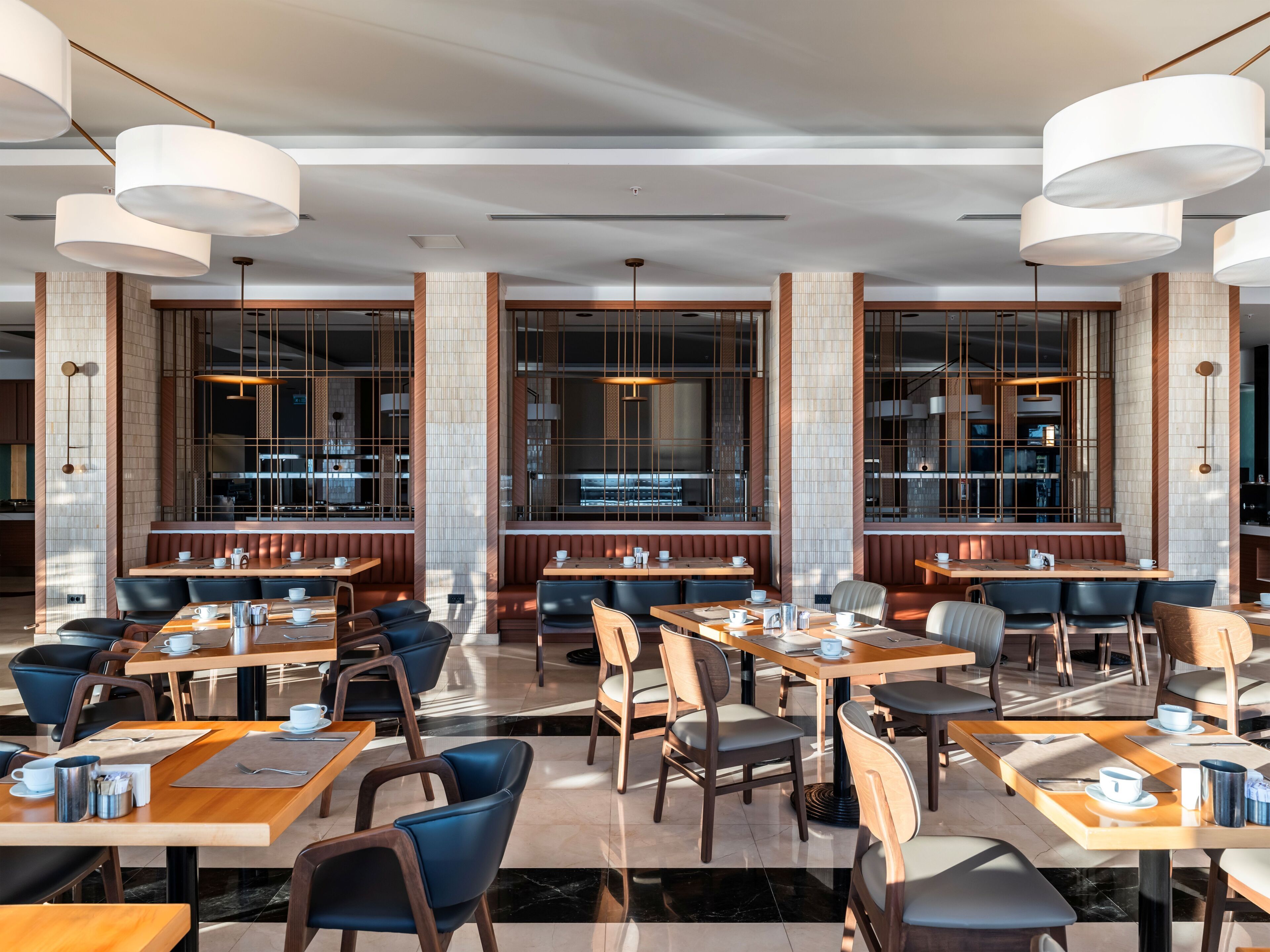 Restaurante moderno com pé direito alto, grandes janelas e diversas opções de assento, incluindo boxes e mesas.