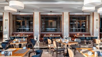 Restaurante moderno com pé direito alto, grandes janelas e diversas opções de assento, incluindo boxes e mesas.