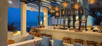 Uma área de bar com assentos, balcão e luminárias pendentes.