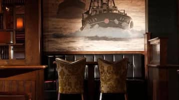 Uma área de bar com uma grande pintura de navio, assentos acolchoados e mobiliário de madeira.