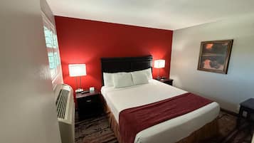 Quarto de hotel com uma cama grande, duas mesas de cabeceira com luminárias, um radiador, uma parede vermelha e um quadro na parede.