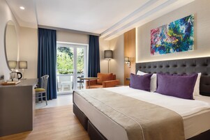 Quarto de hotel moderno com uma cama grande, uma escrivaninha com luminária, uma cadeira e vista para o exterior.