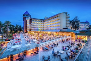 Um hotel com vários andares, áreas de refeições ao ar livre e uma piscina.