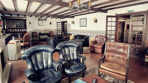 Quarto amplo com vigas de madeira, um candelabro e poltronas de couro.
