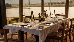 Mesa de jantar posta para refeição, vista para um lago e colinas ao fundo.