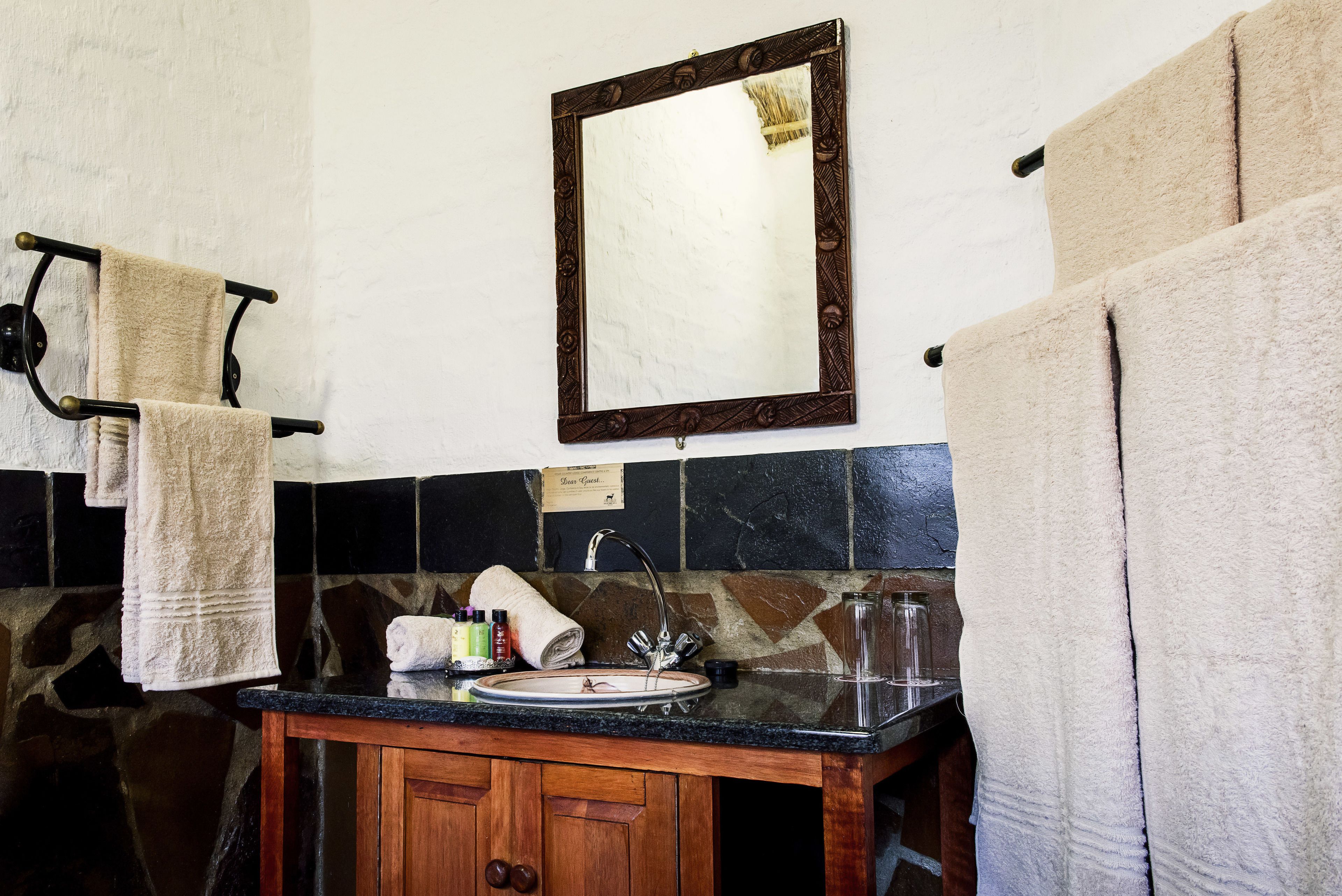 Casa de banho com painel de parede em pedra, toucador de madeira, espelho e toalhas num suporte.