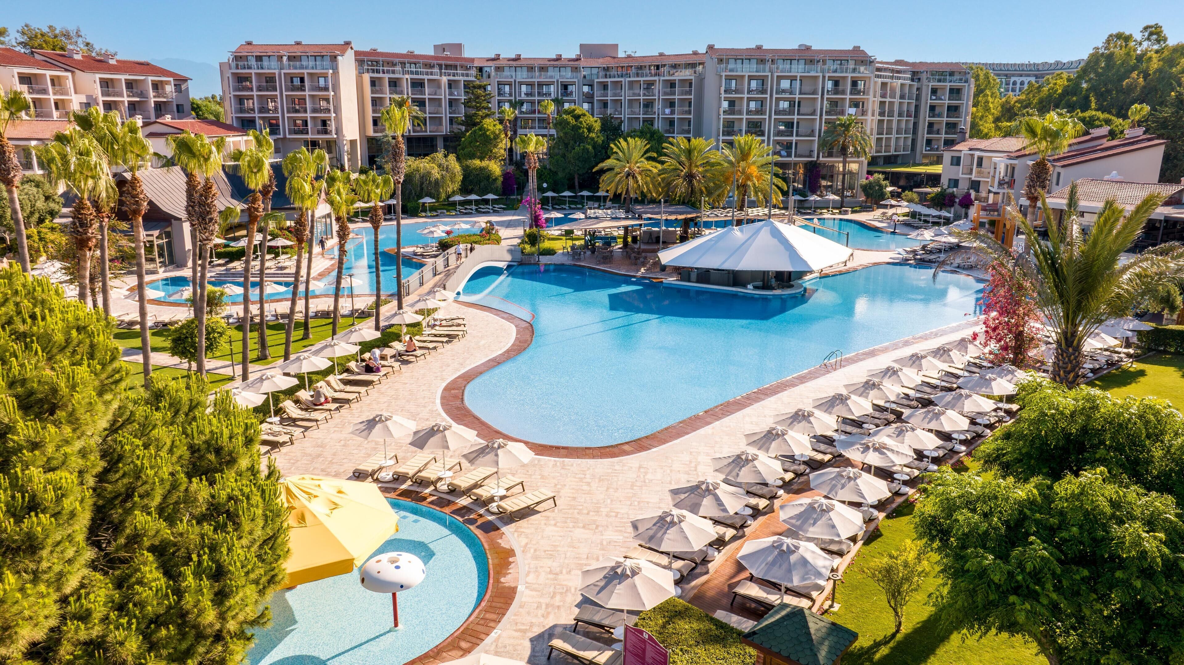 Resort com várias piscinas, espreguiçadeiras e palmeiras.