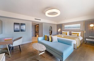 Quarto de hotel moderno com cama, sofá, mesa de jantar e uma mesinha.