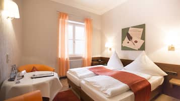Quarto de hotel com cama, mesa com cadeira, janela com cortinas, luminária na parede e quadro emoldurado na parede.