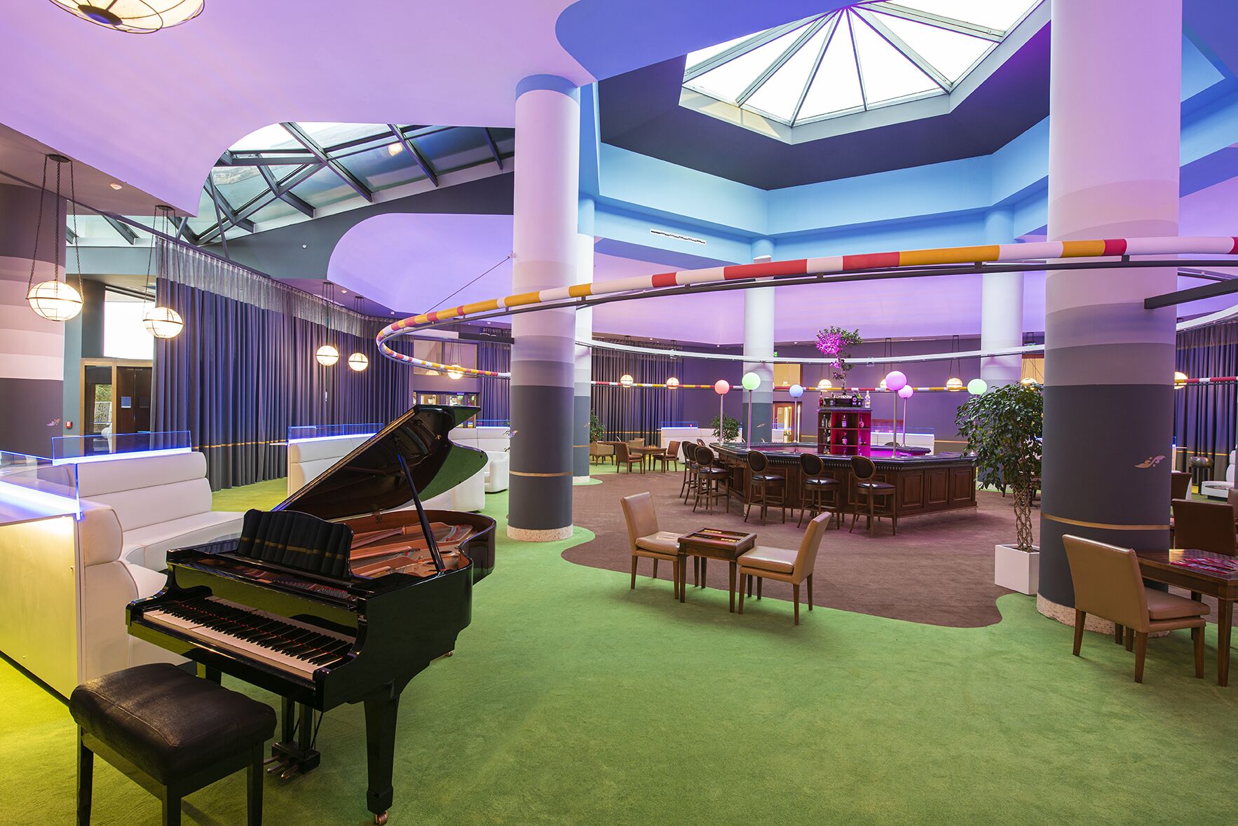 Um hall amplo com um piano de cauda, área de bar e teto alto com claraboias.