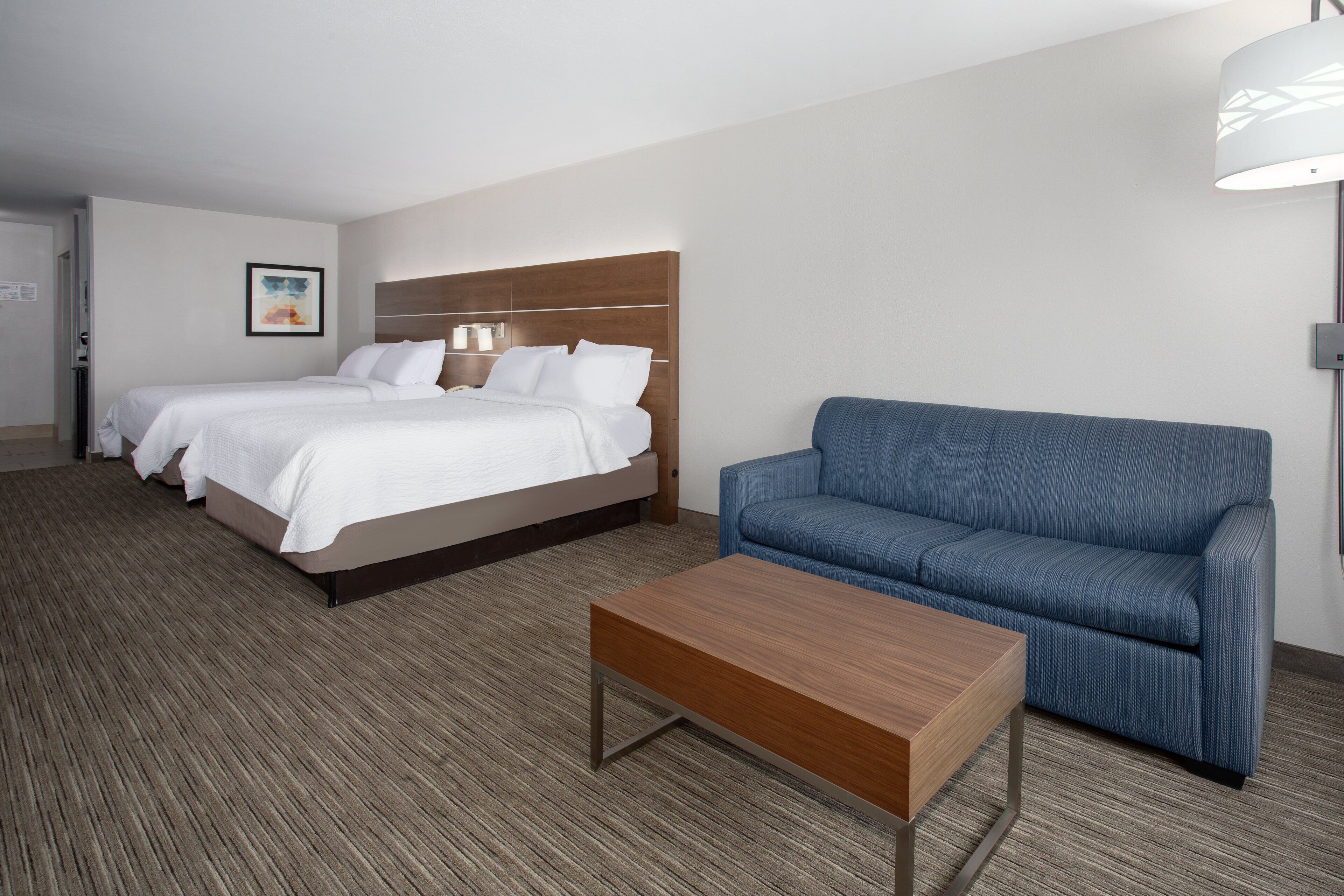 Quarto de hotel com duas camas, um sofá e uma mesa pequena.