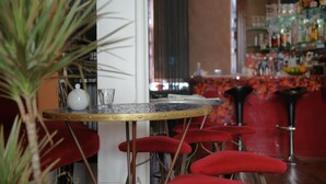 Uma área de bar com banquetas vermelhas, uma mesa redonda com uma jarra branca e um copo.
