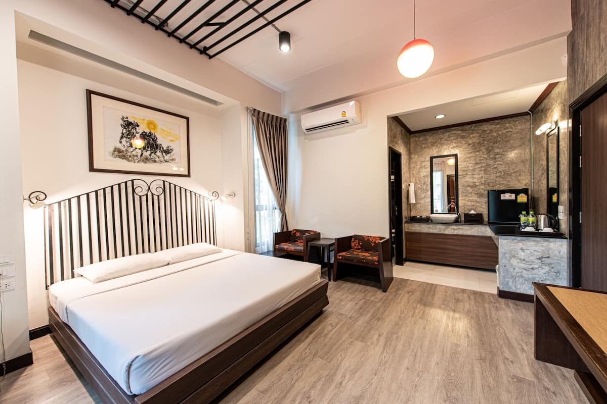 Quarto de hotel moderno com uma cama grande, uma escrivaninha, duas cadeiras, um banheiro com espelho e um ar condicionado.