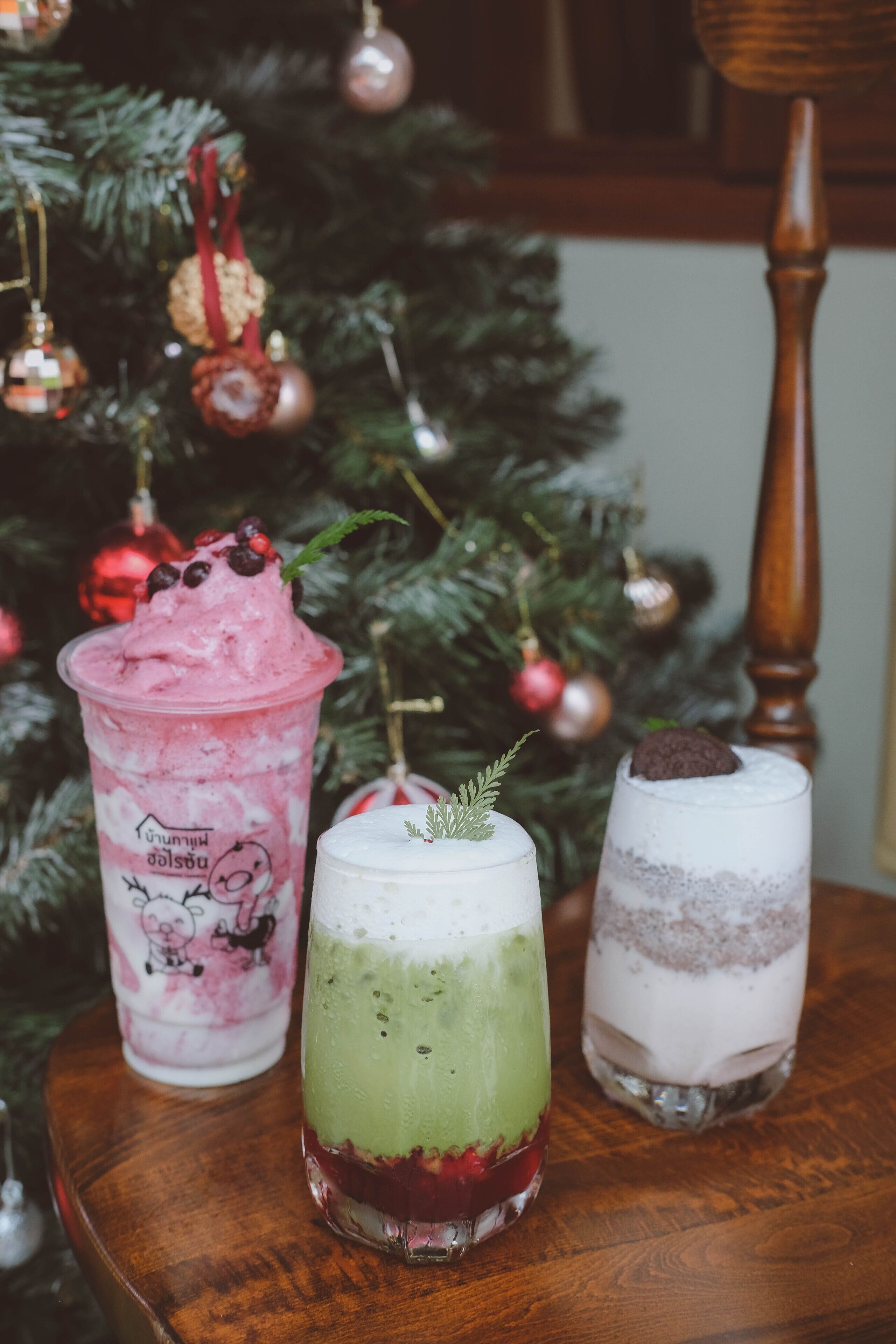 Três bebidas dispostas em camadas sobre uma mesa de madeira, com uma árvore de Natal ao fundo.