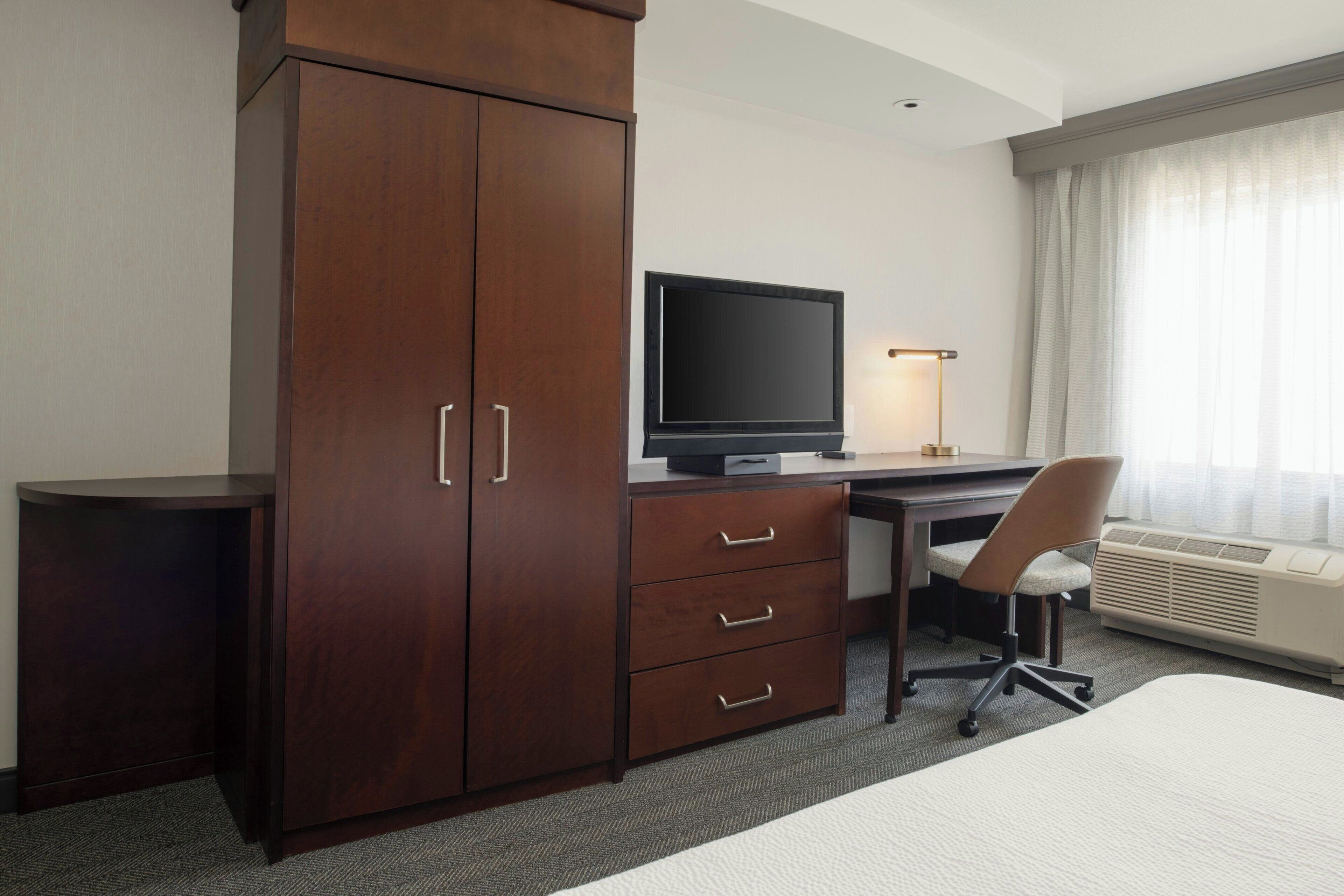 Quarto de hotel com guarda-roupa de madeira, mesa com televisão de tela plana, cadeira e cama.