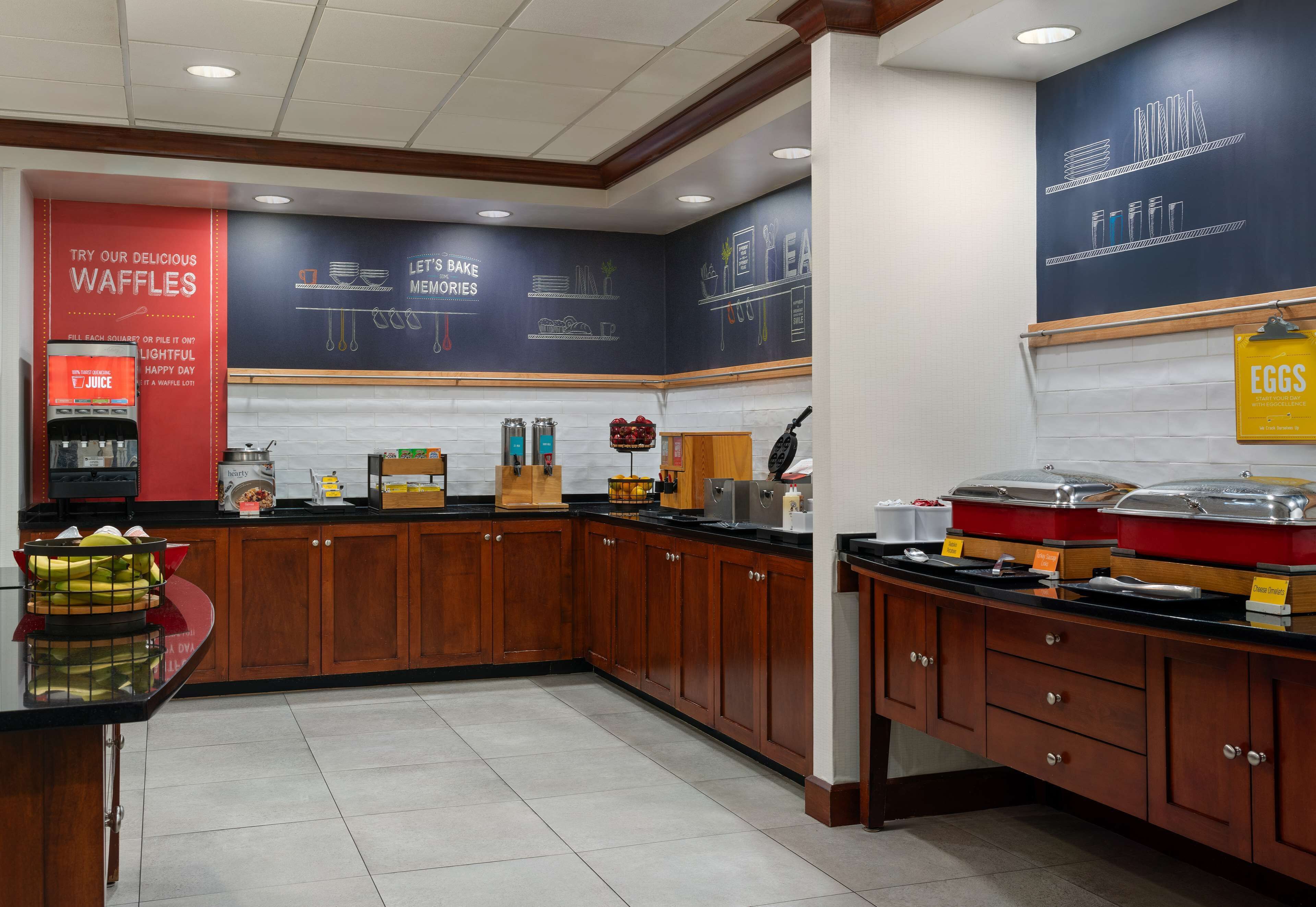 Uma área de cozinha com estação de waffles, dispensador de sucos e diversos eletrodomésticos.