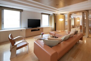 Quarto de hotel moderno com sofá, poltrona e televisão de tela plana.