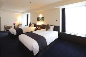 Quarto de hotel com duas camas, uma escrivaninha, uma cadeira e uma janela com cortinas.