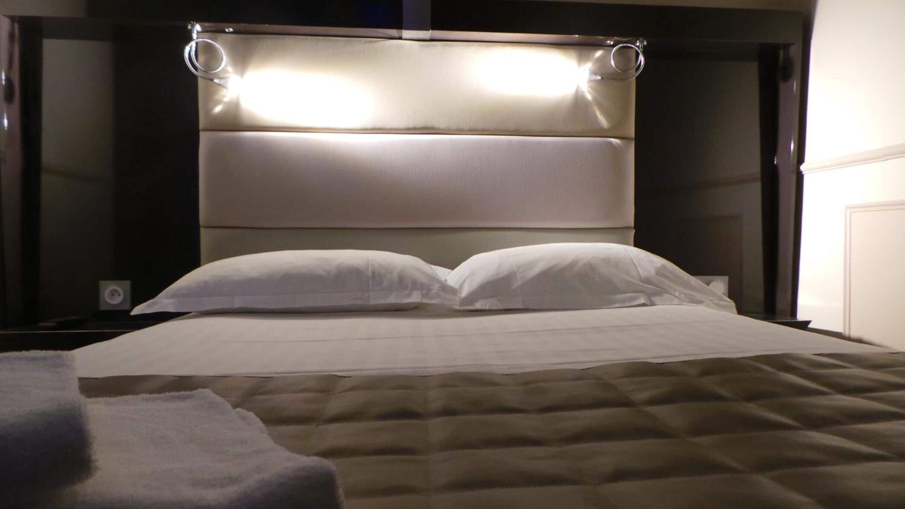 Cama bem arrumada com cabeceira, dois travesseiros e um cobertor.