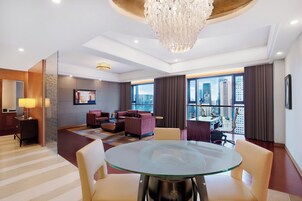 Quarto de hotel moderno com mesa de vidro, assentos confortáveis, um lustre e vista para a cidade.