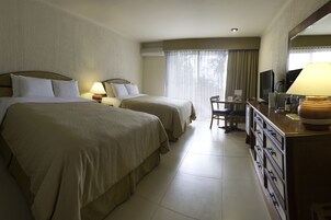 Quarto de hotel com duas camas, uma escrivaninha com cadeira, televisão e cómoda.